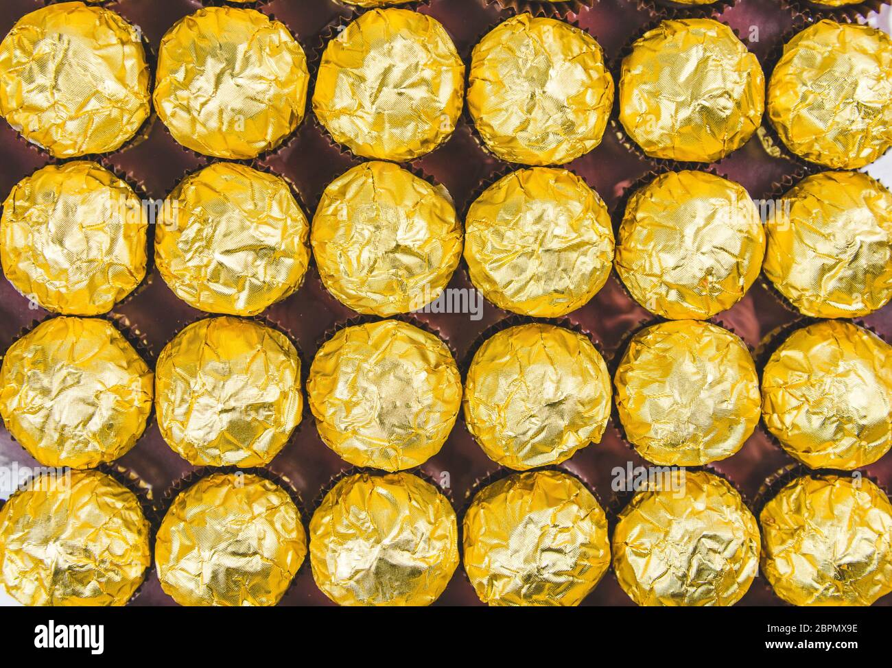 a lot of shiny golden chocolate wrapper in line on white background ...