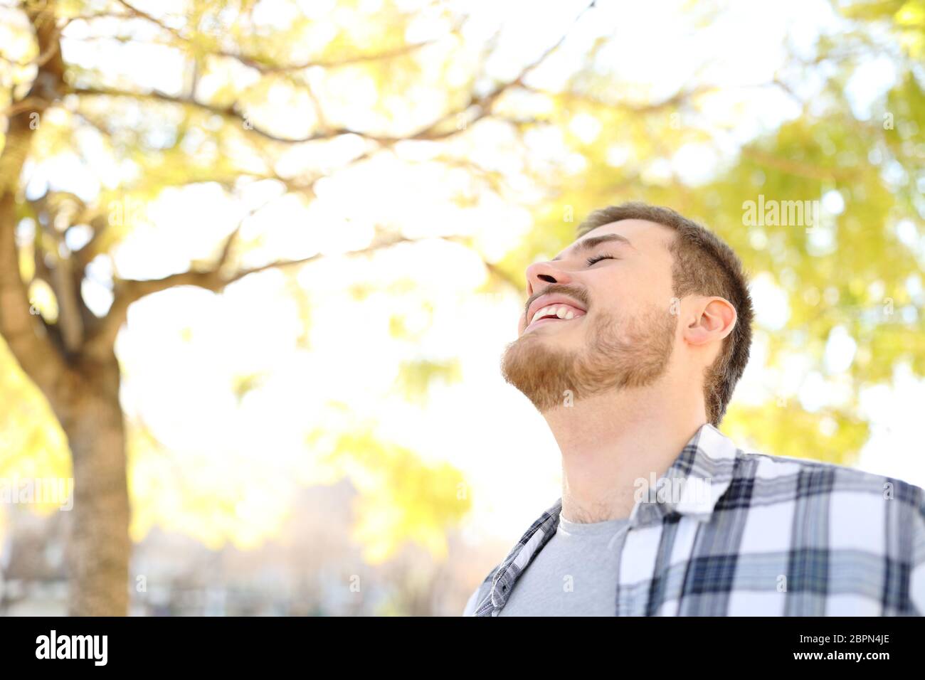 Happy man is breathing fresh air in a park with trees in the background ...