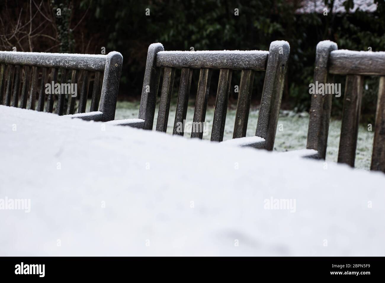 Wooden cozy garden chairs covered in snow in a backyard garden. winter ...