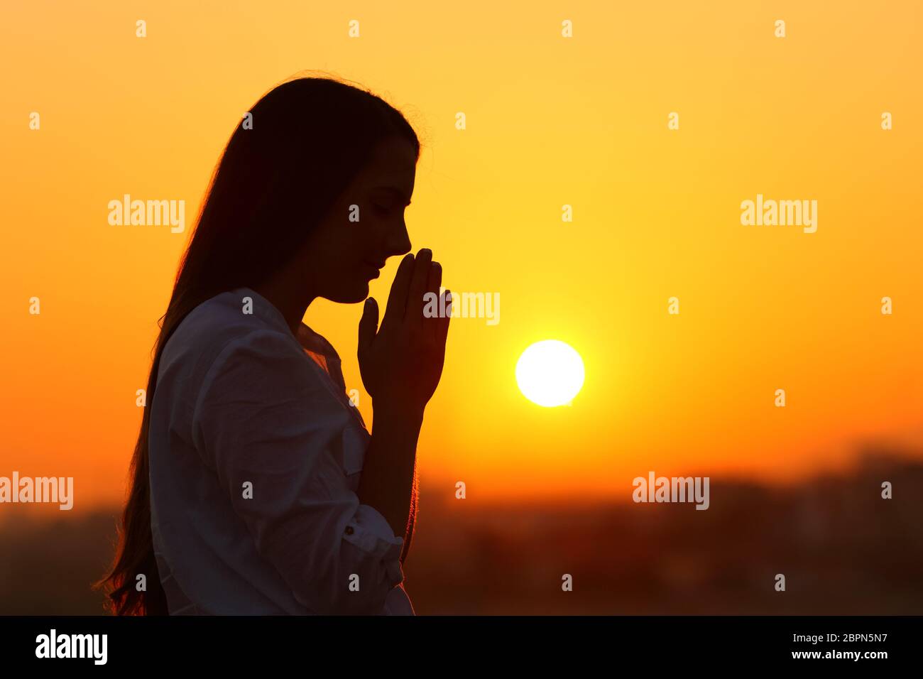 Side view backlight portrait of a woman silhouette praying at sunset ...