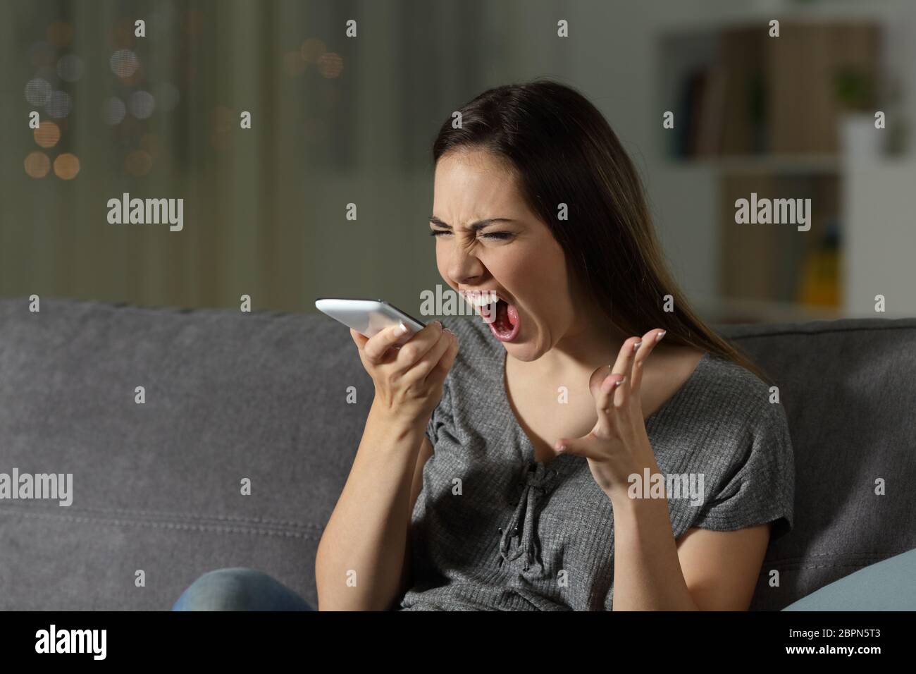 Angry woman shouting at the smart phone sitting on a couch in the ...