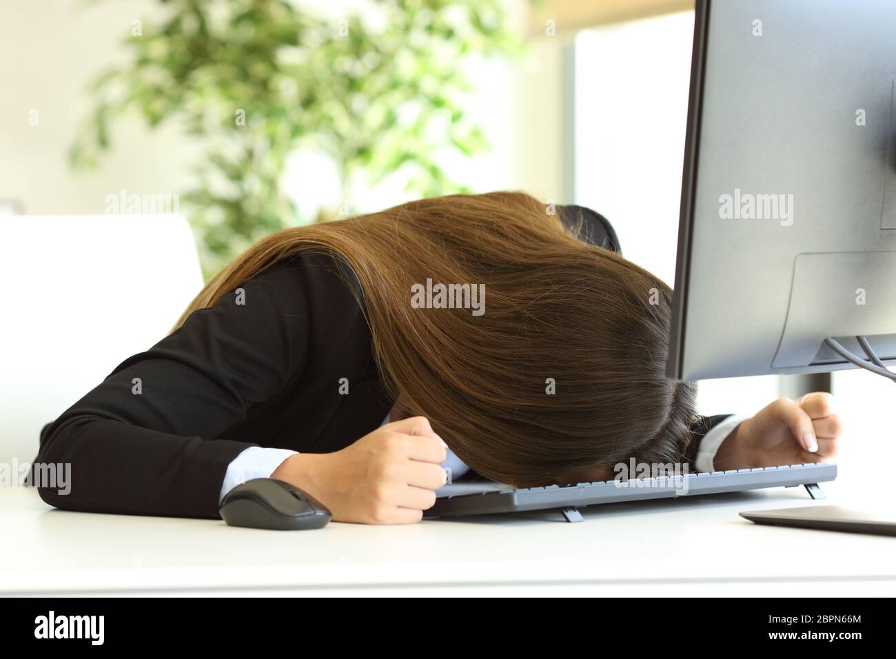 Frustrated businesswoman banging head against the desktop in front of a ...