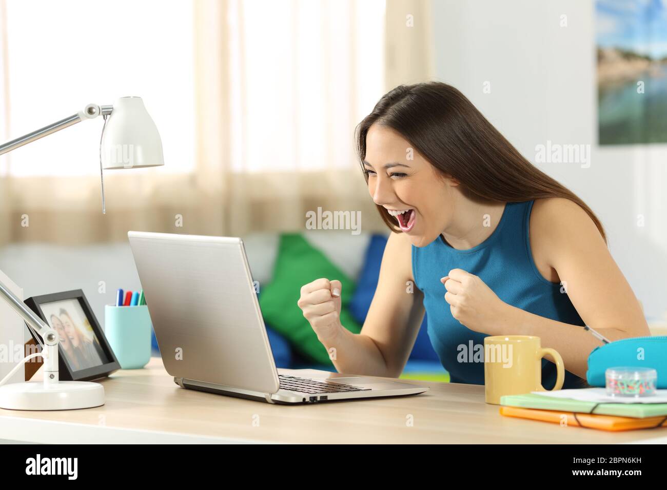 Single excited student on line with a laptop sitting in a desk in her ...