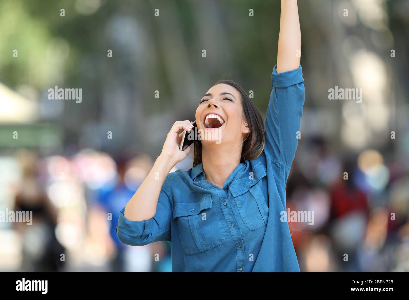 Excited woman receiving good news on the phone raising arms on the ...