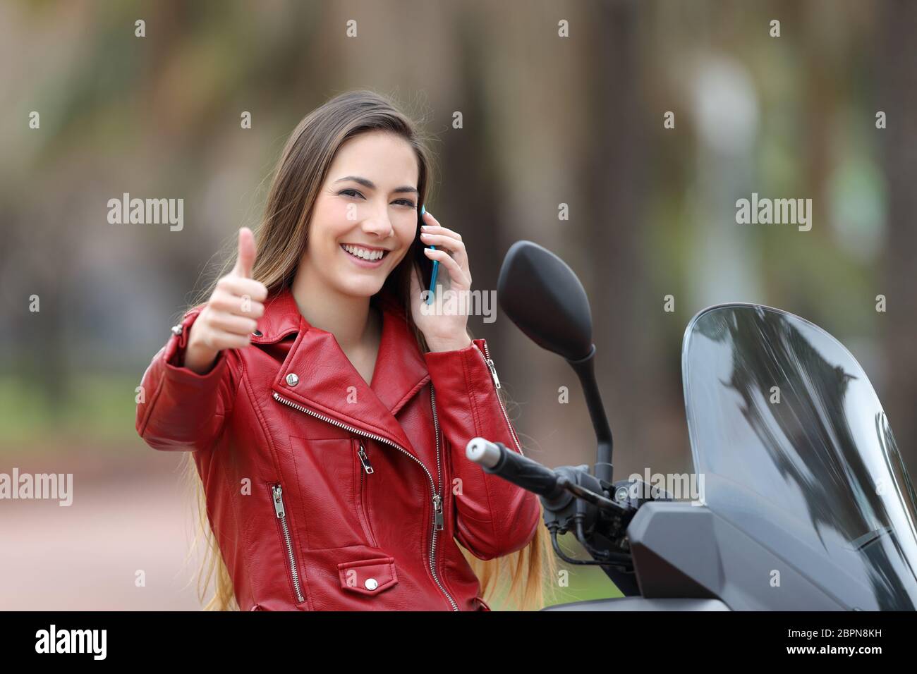 Happy biker sitting on a motorbike with thumbs up calling on phone on ...