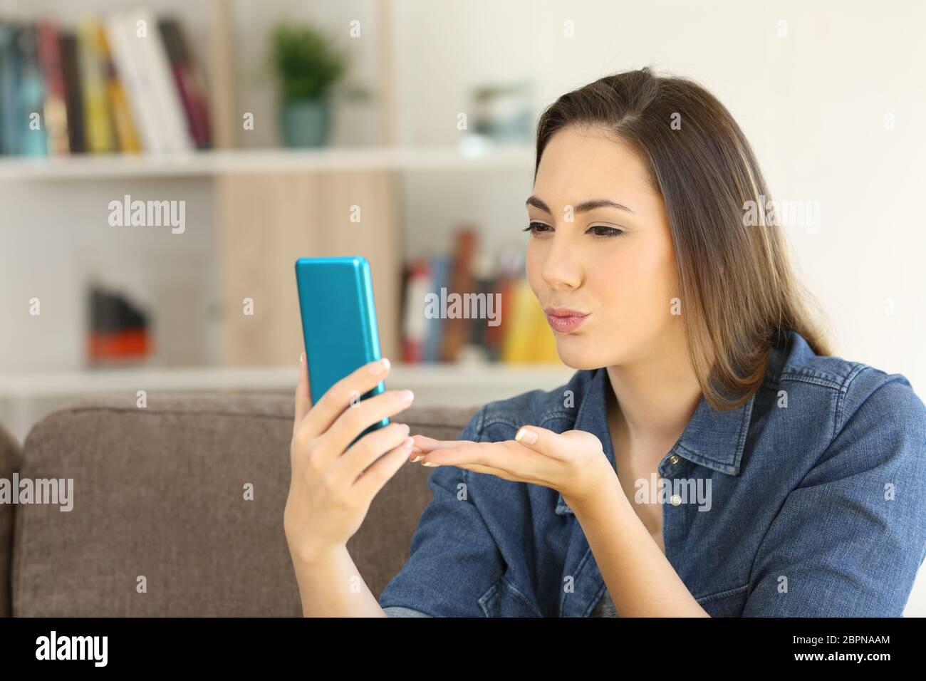 Woman sending a kiss online during a video call with a smart phone ...