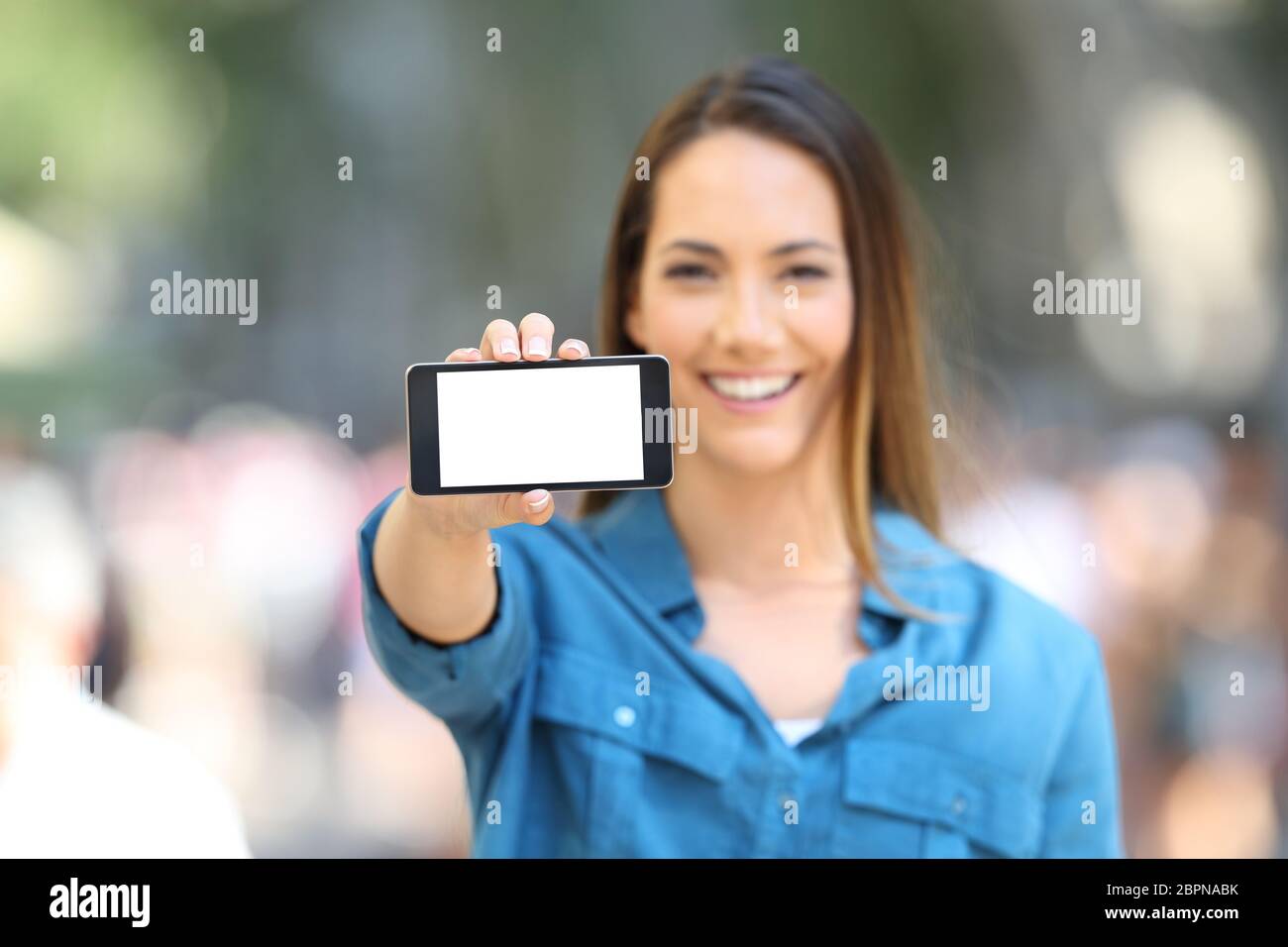 Woman showing a blank horizontal phone screen mock up on the street ...