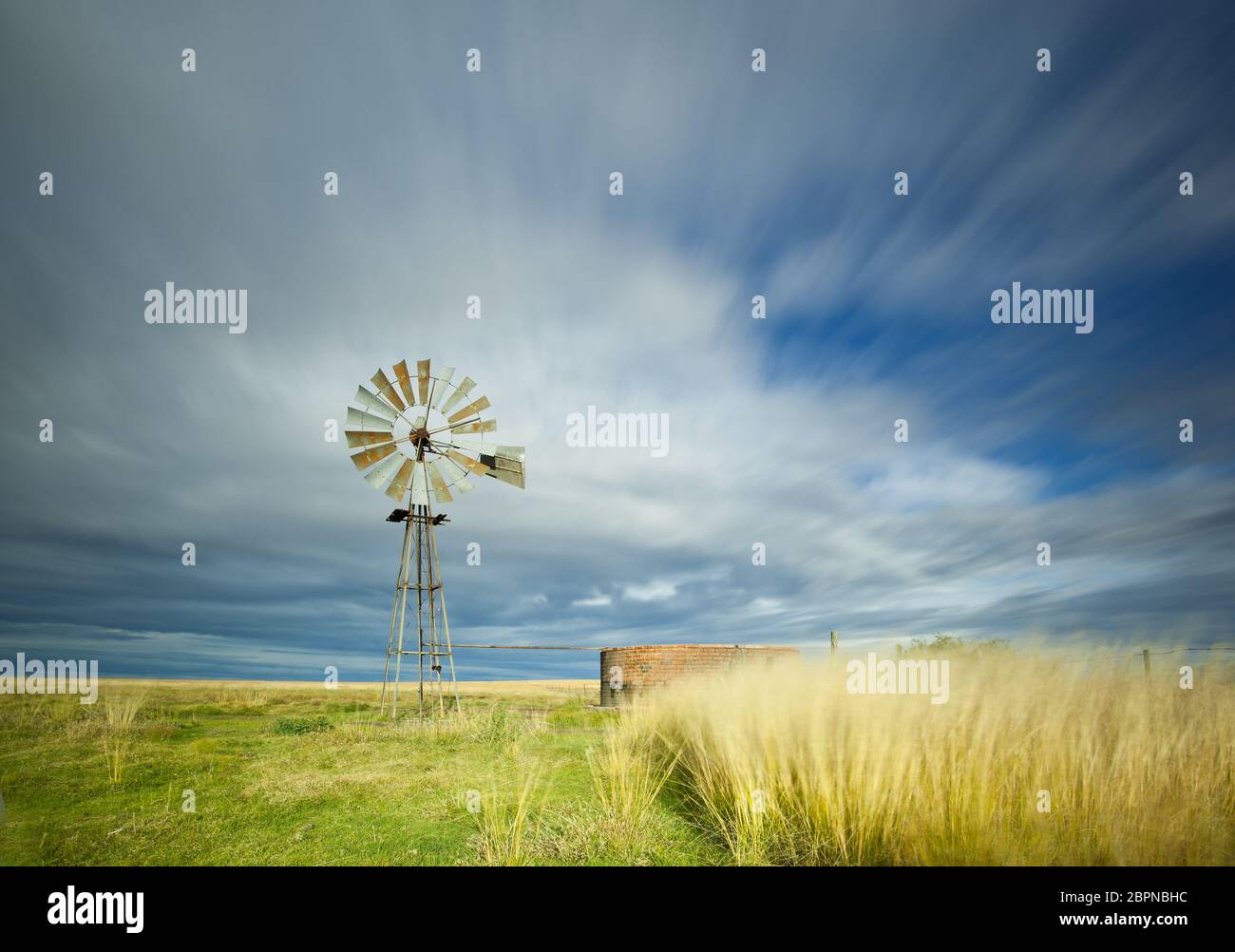 long exposure image with windmill and dam and streaky clouds overhead ...