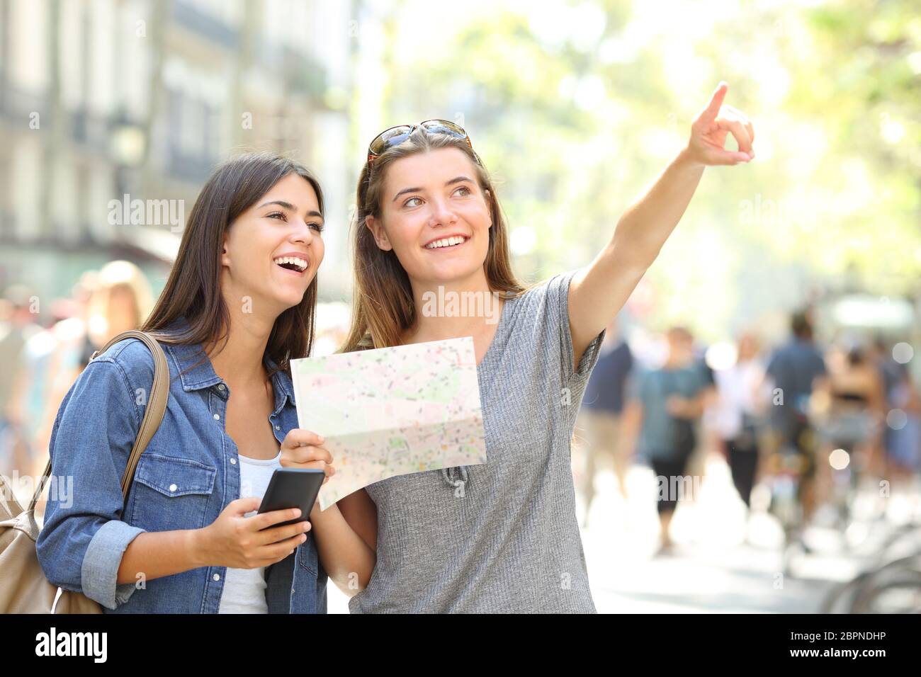 Two happy tourists sightseeing holding a map and pointing up in the ...