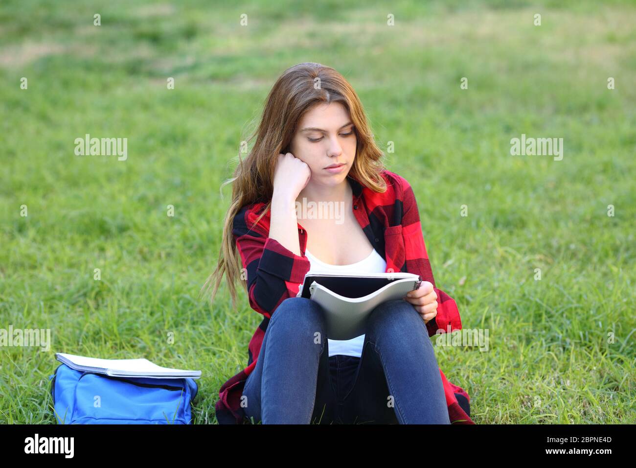 Serious student studying reading notes sitting on the grass in a campus ...