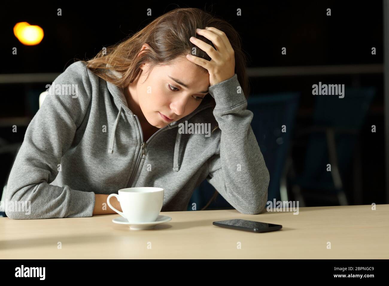 Portrait of a sad teen waiting for a smart phone message sitting in a ...