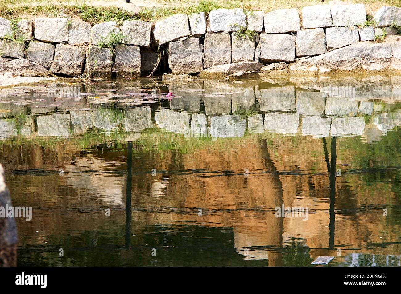Stone block wall and its reflection in water of pond Stock Photo - Alamy