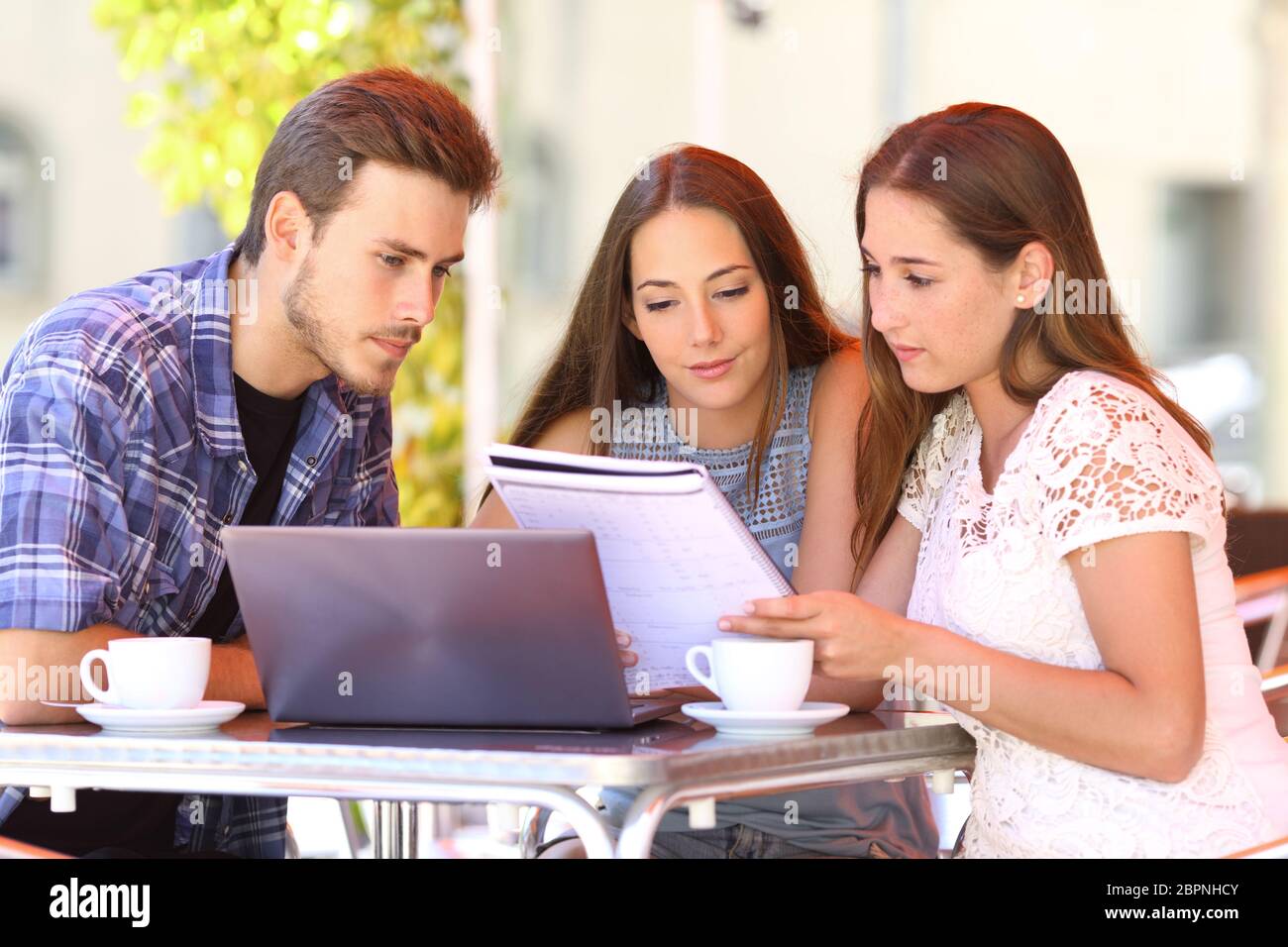 Three happy students learning together reading notes in a coffee shop ...