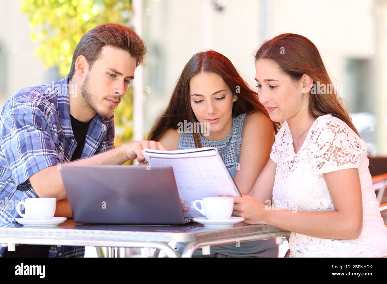 Three concentrated students studying comparing notes in a coffee shop ...