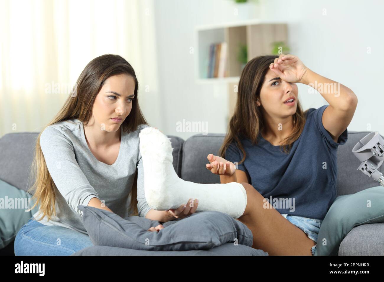 Angry woman helping her dramatic disabled roommate sitting on a couch ...