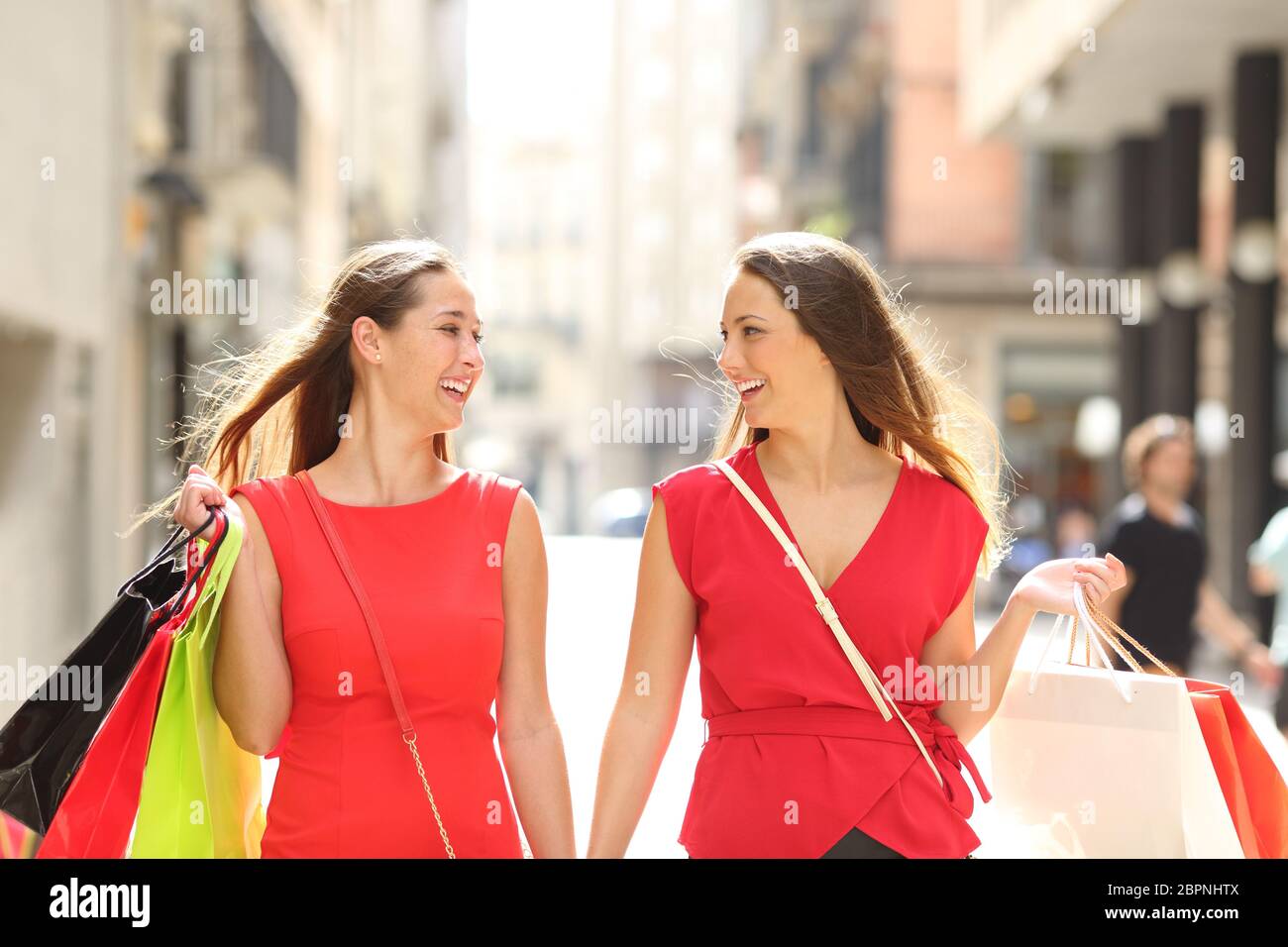 Front view of two fashion happy shoppers in red talking holding ...
