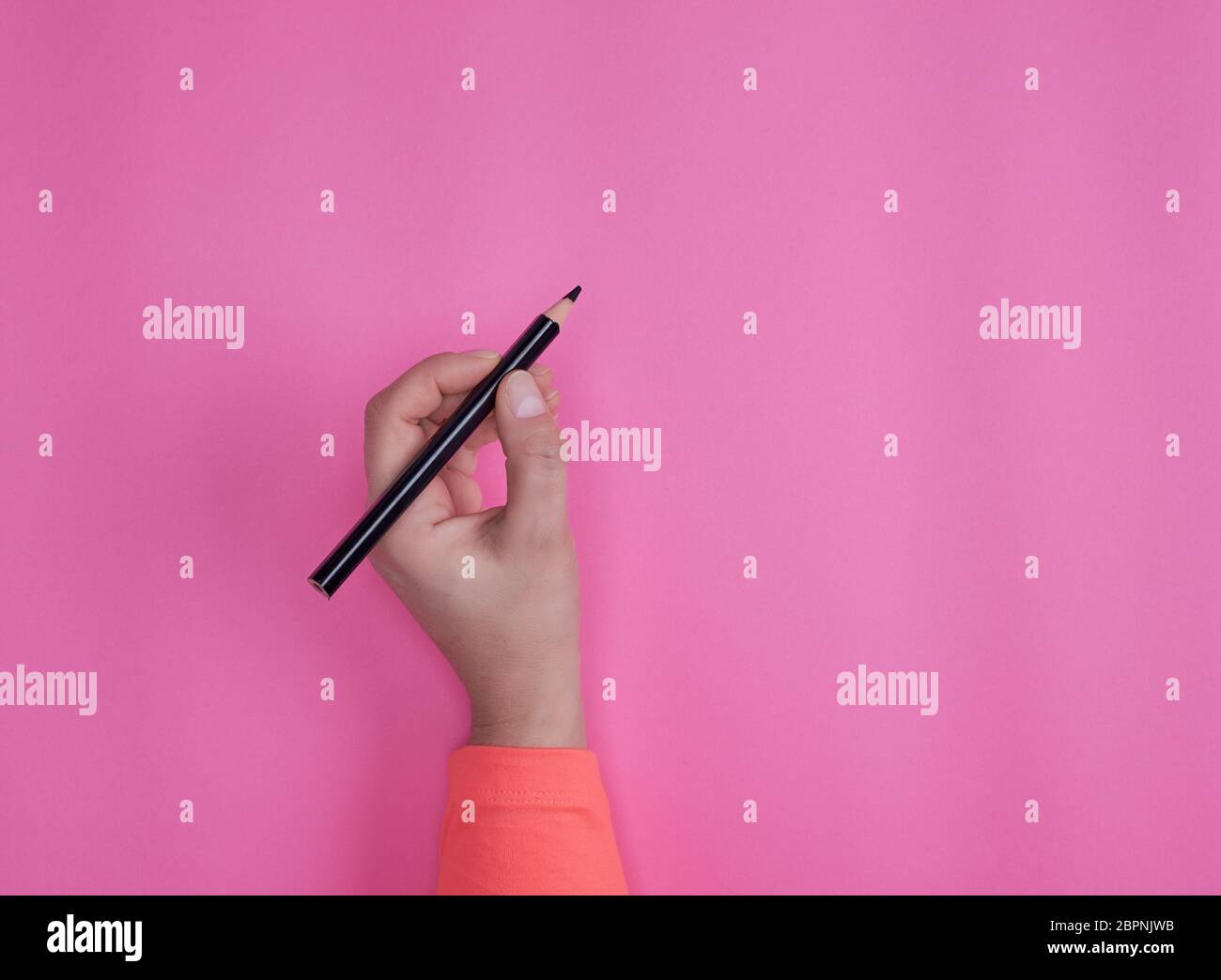 black wooden pencil in a female hand on a pink background, copy space ...