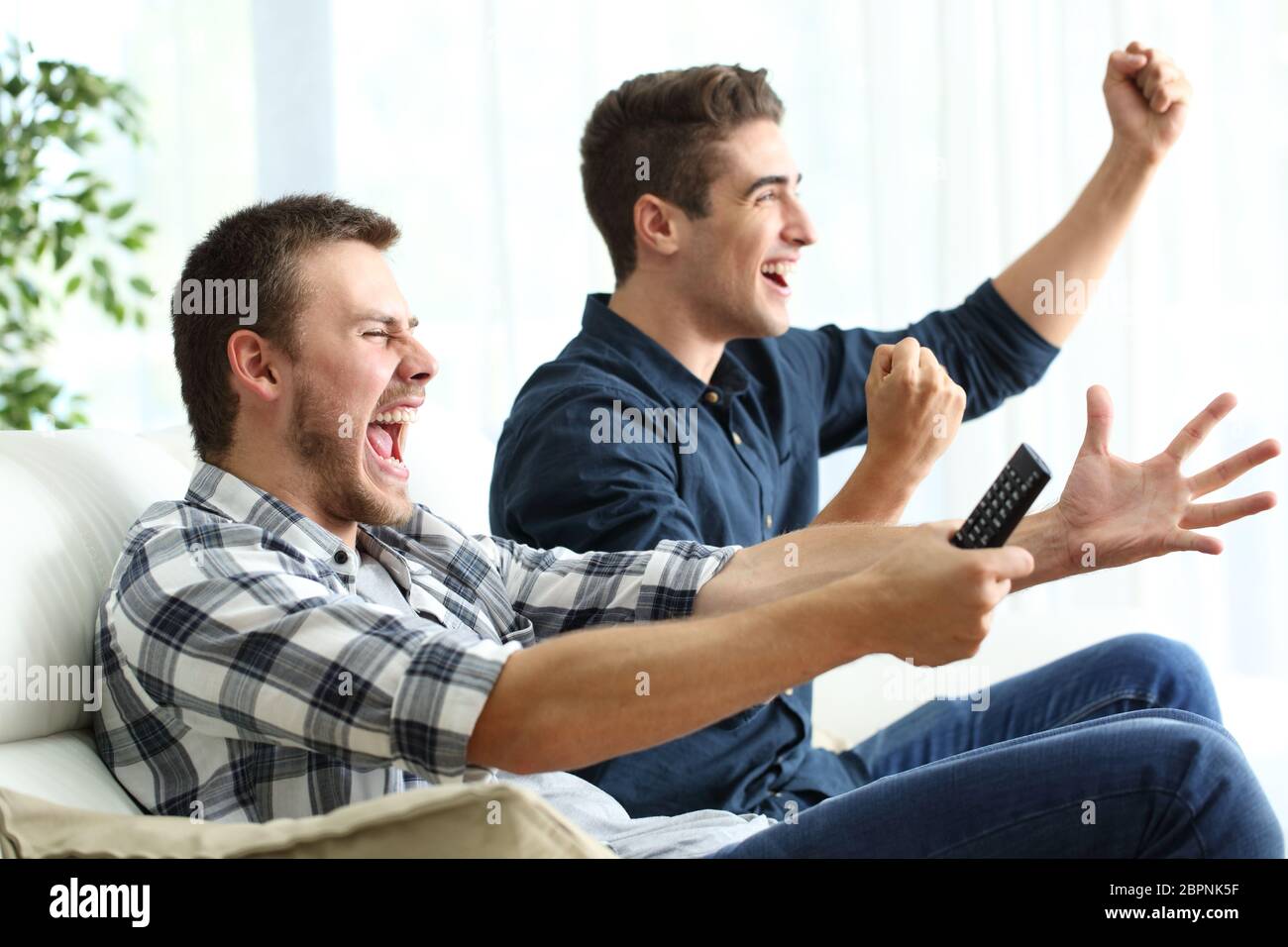 Two excited roommates watching tv together sitting on a couch in the ...