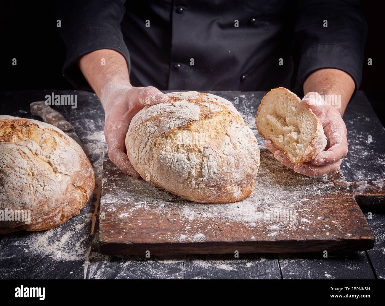 cook in a black tunic holds fresh baked round bread, close up Stock ...