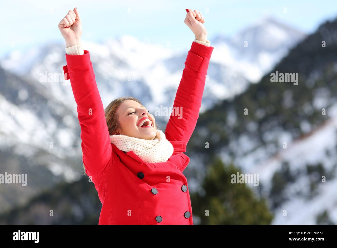 Excited woman wearing a red jacket raising arms in a snowy mountain in ...