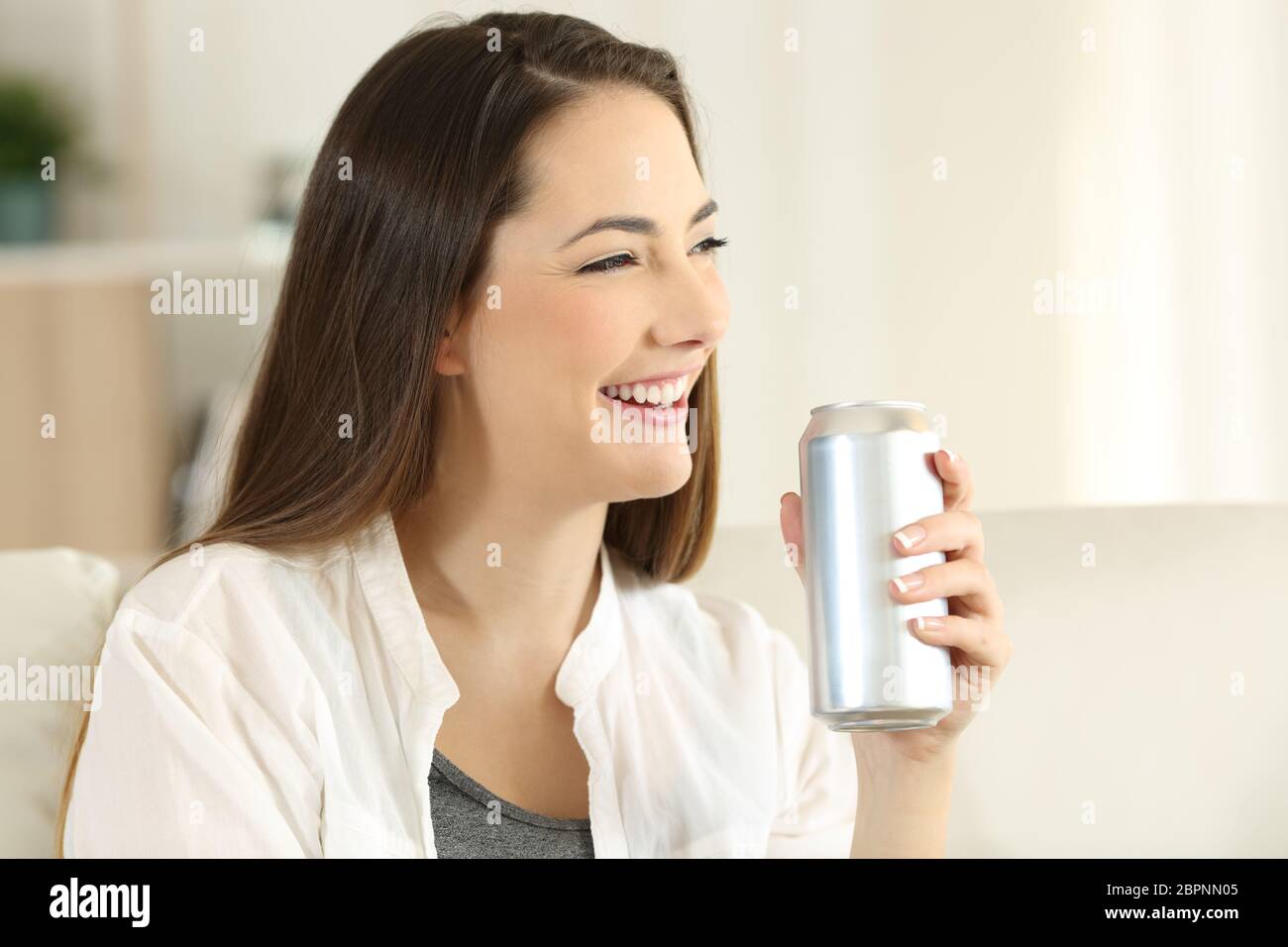 Portrait of a woman holding a soda can sitting on a couch in the living ...