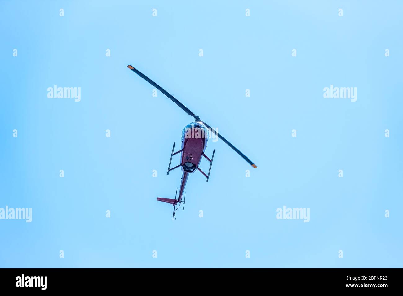 A small two seater commercial helicopter set against a clear, blue sky ...