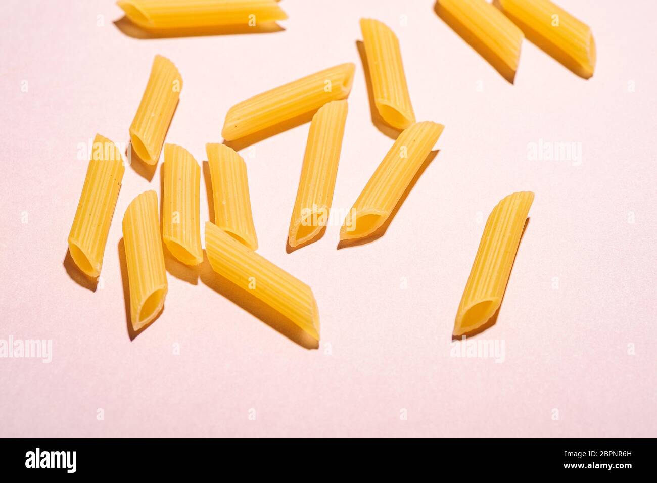 Italian pasta, raw penne tube macaroni on pink pastel background, angle ...