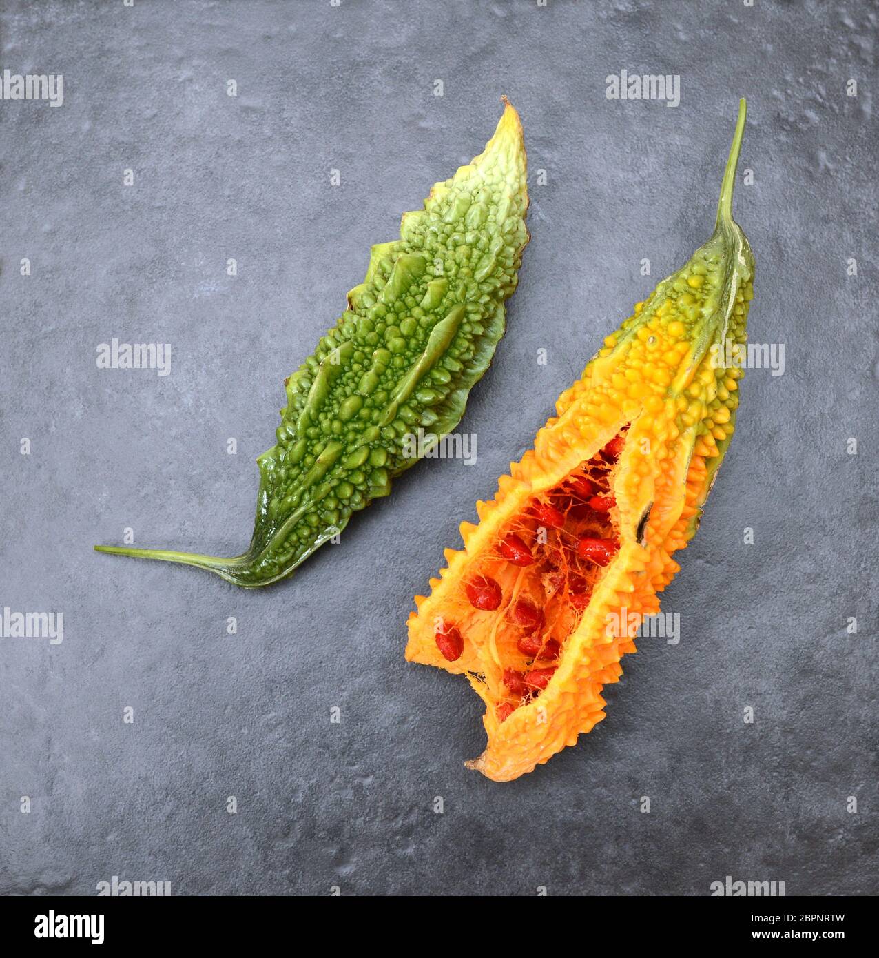 Two bitter melons - with green ridged skin and overripe orange flesh ...