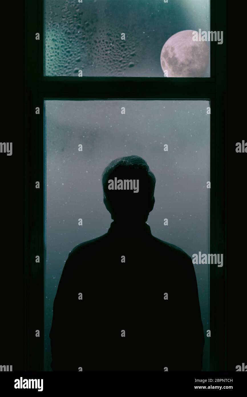 silhouette of man observing the full moon from inside his house during ...