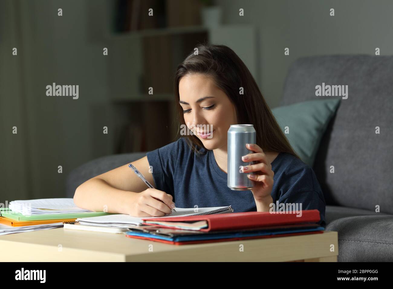 Happy student taking notes holding energy drink in the night at home ...
