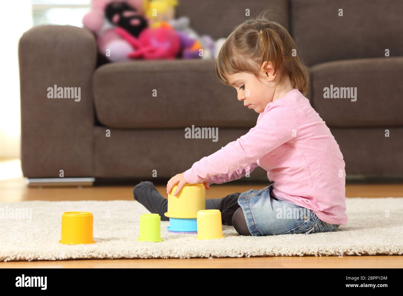 Side view of a kid playing with toys sitting on the floor of the living ...