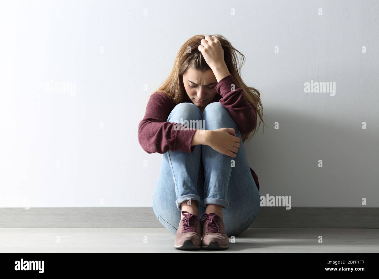 Front view full body portrait of a sad woman sitting on the floor at ...