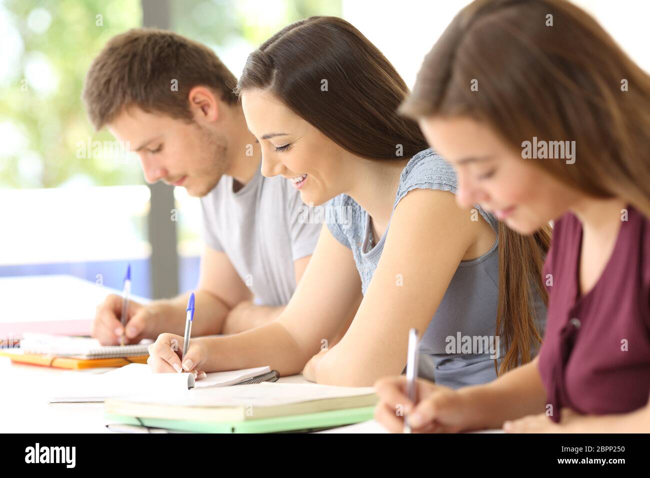 Three students studying taking notes during a class in a classroom ...