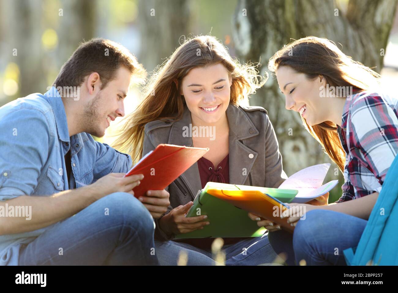Three students learning reading notes together sitting on the grass in ...