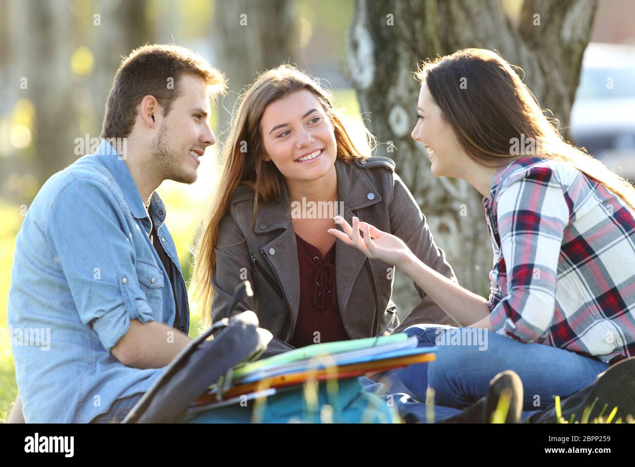 Three students talking after classes beside books and ruckpacks sitting ...