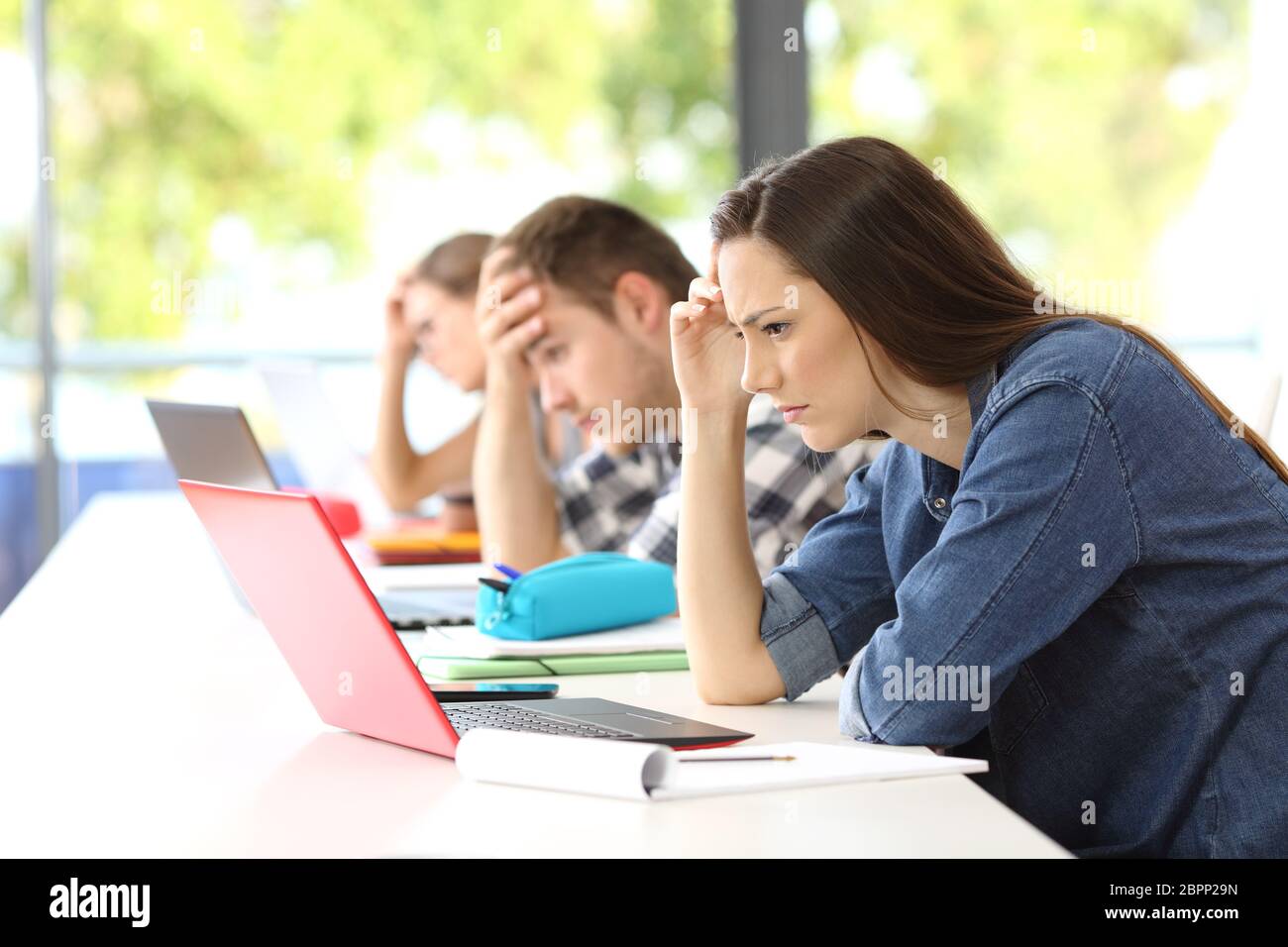 Three worried students trying to do a difficult work on line sitting in ...