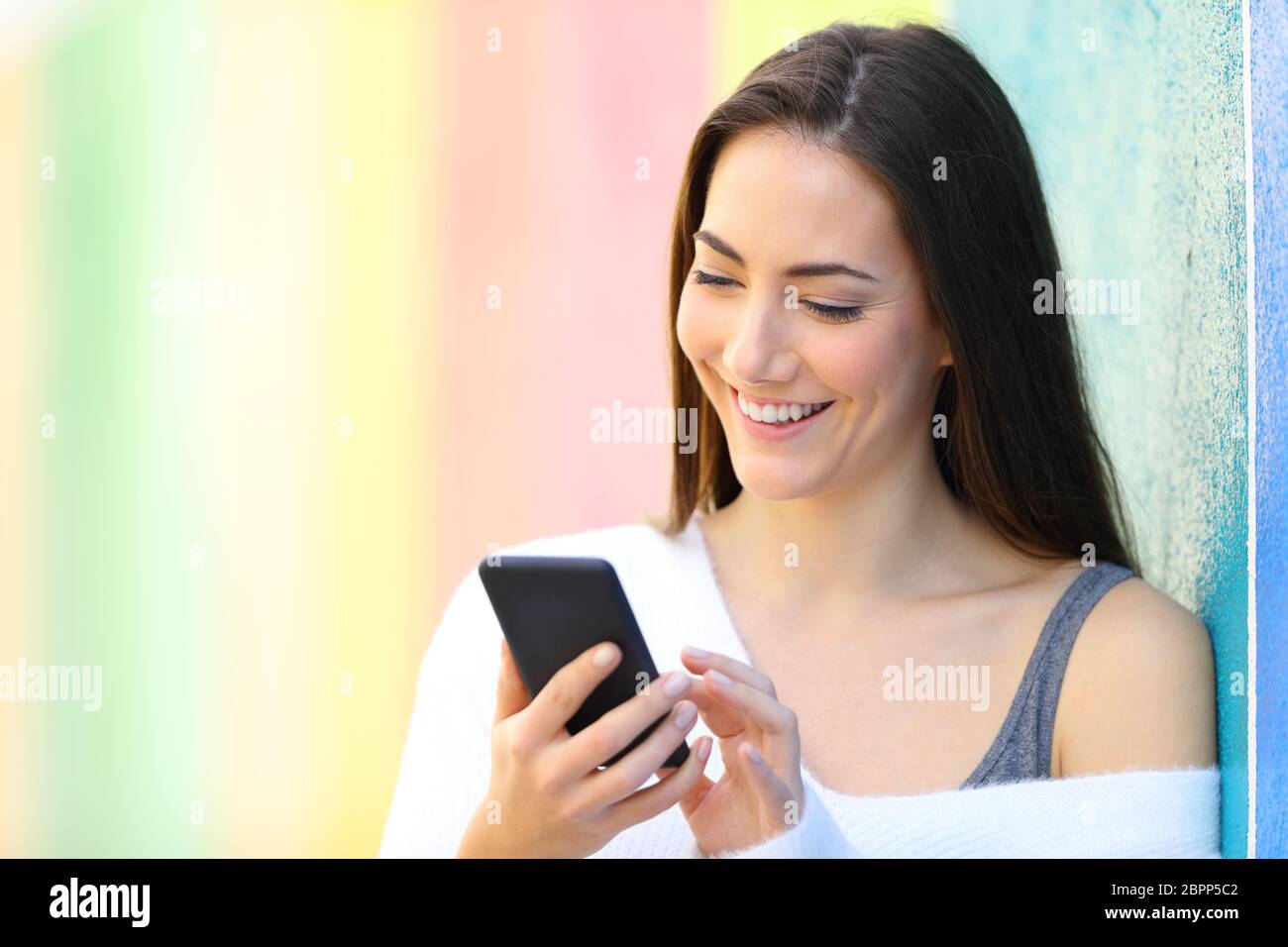 Happy woman is browsing smart phone content beside a colorful wall in ...