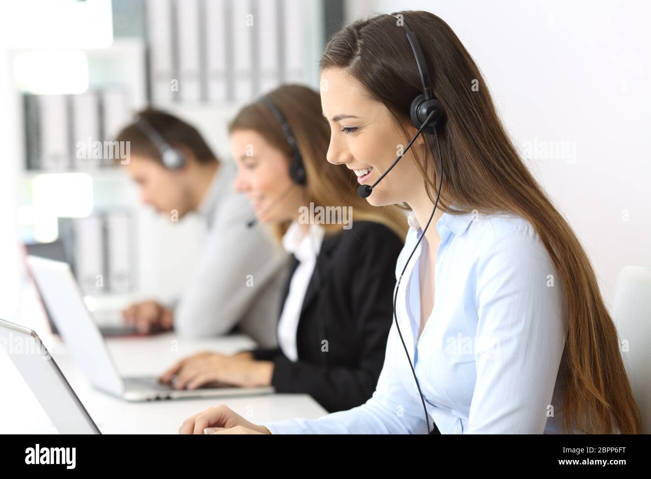 Side view of a telemarketer working on line at office with other ...