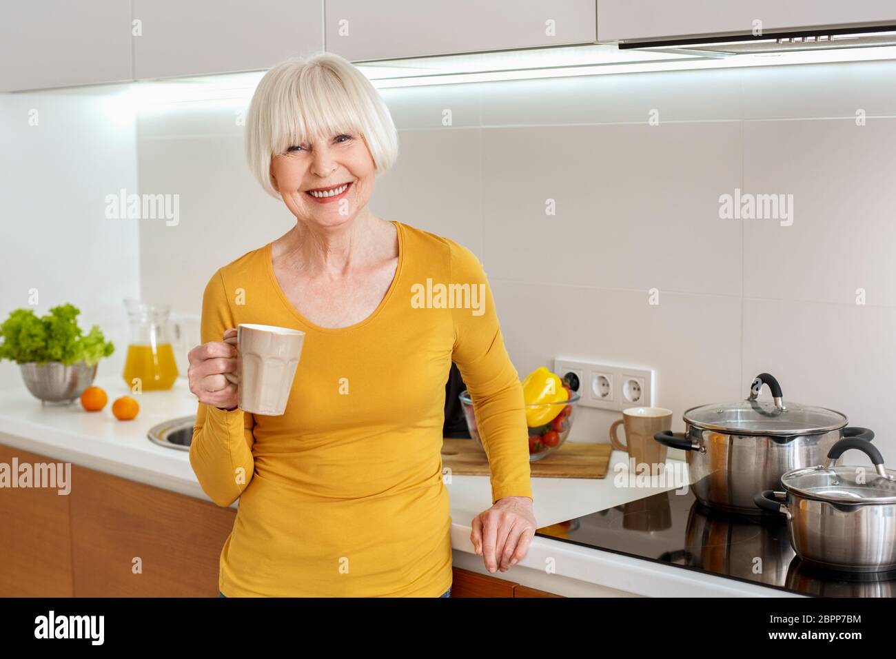 Retirement. Senior woman standing at kitchen drinking hot coffee ...