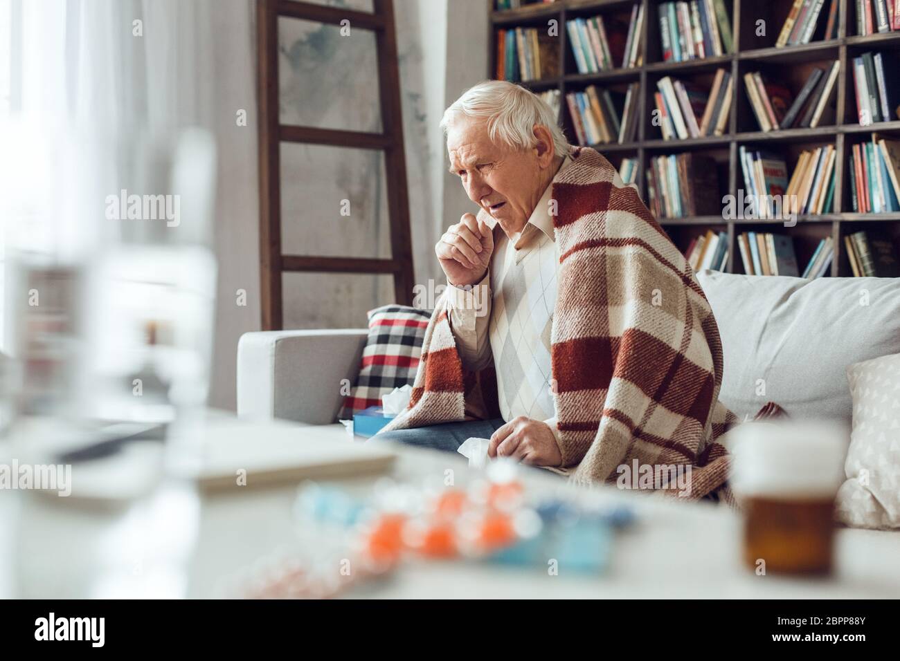 Senior man alone sitting at library covered with plaid coughing Stock ...
