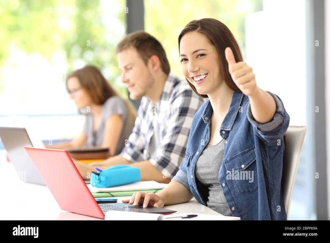 Proud student posing with thumbs up at classroom with classmates in the ...