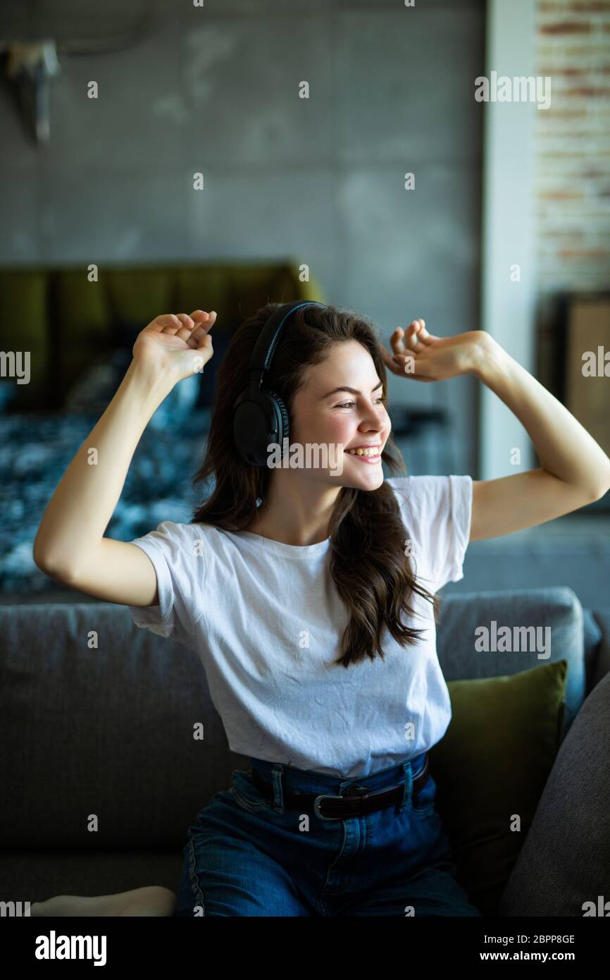Image of cute smiling woman dancing on couch while using wireless ...