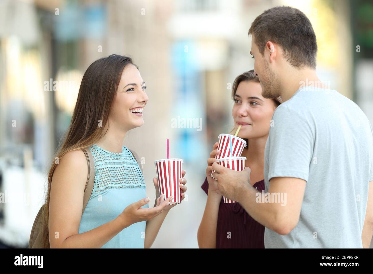 Three happy friends talking and drinking takeaway refreshments standing ...