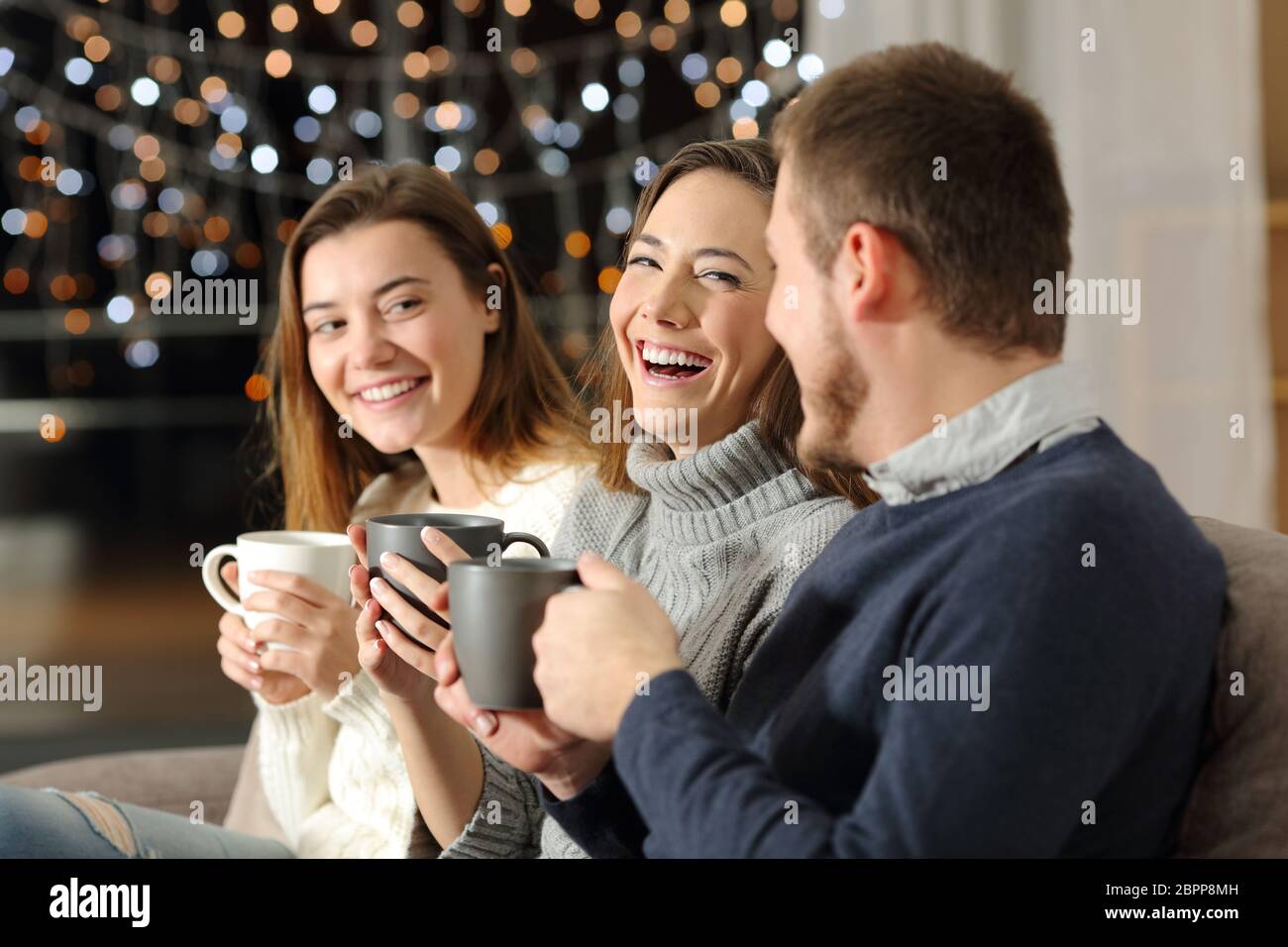 Three friends talking and laughing in the night sitting on a couch in ...