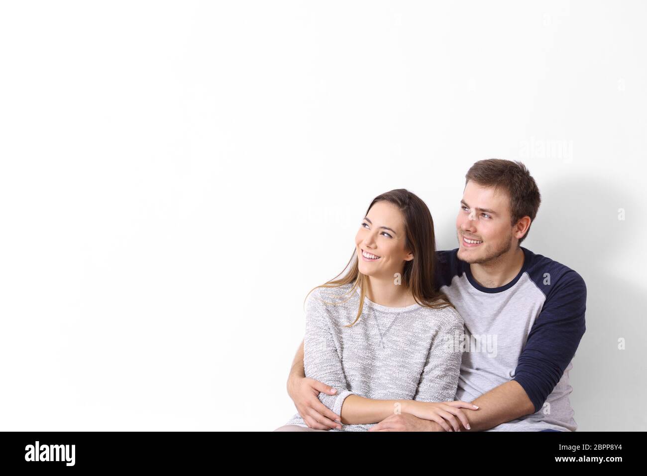 Front view of a happy couple looking at side on a white wall Stock ...