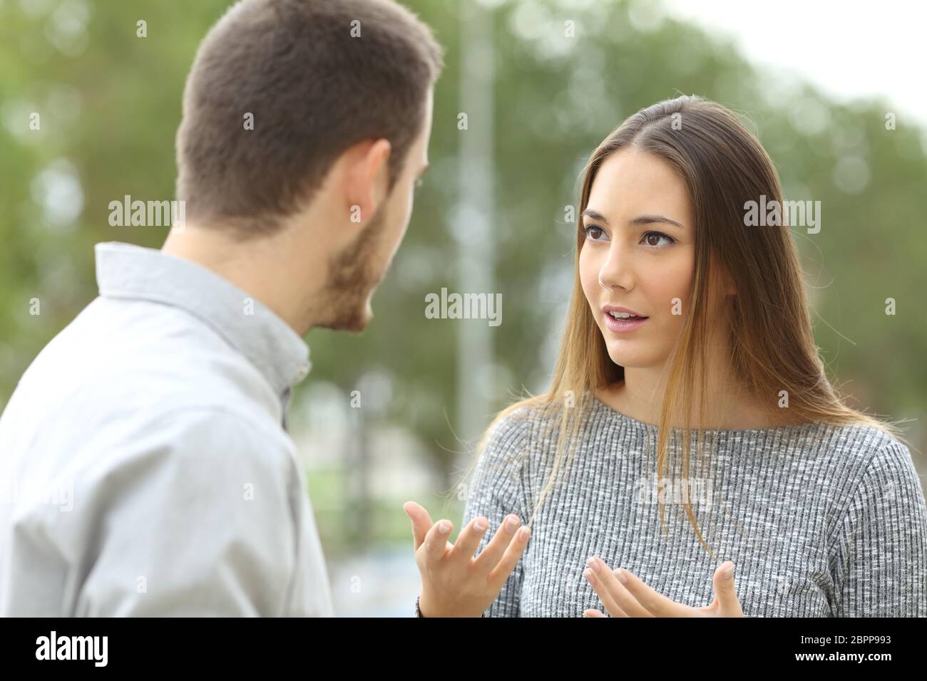 Couple talking outdoors in a park with a green background Stock Photo ...