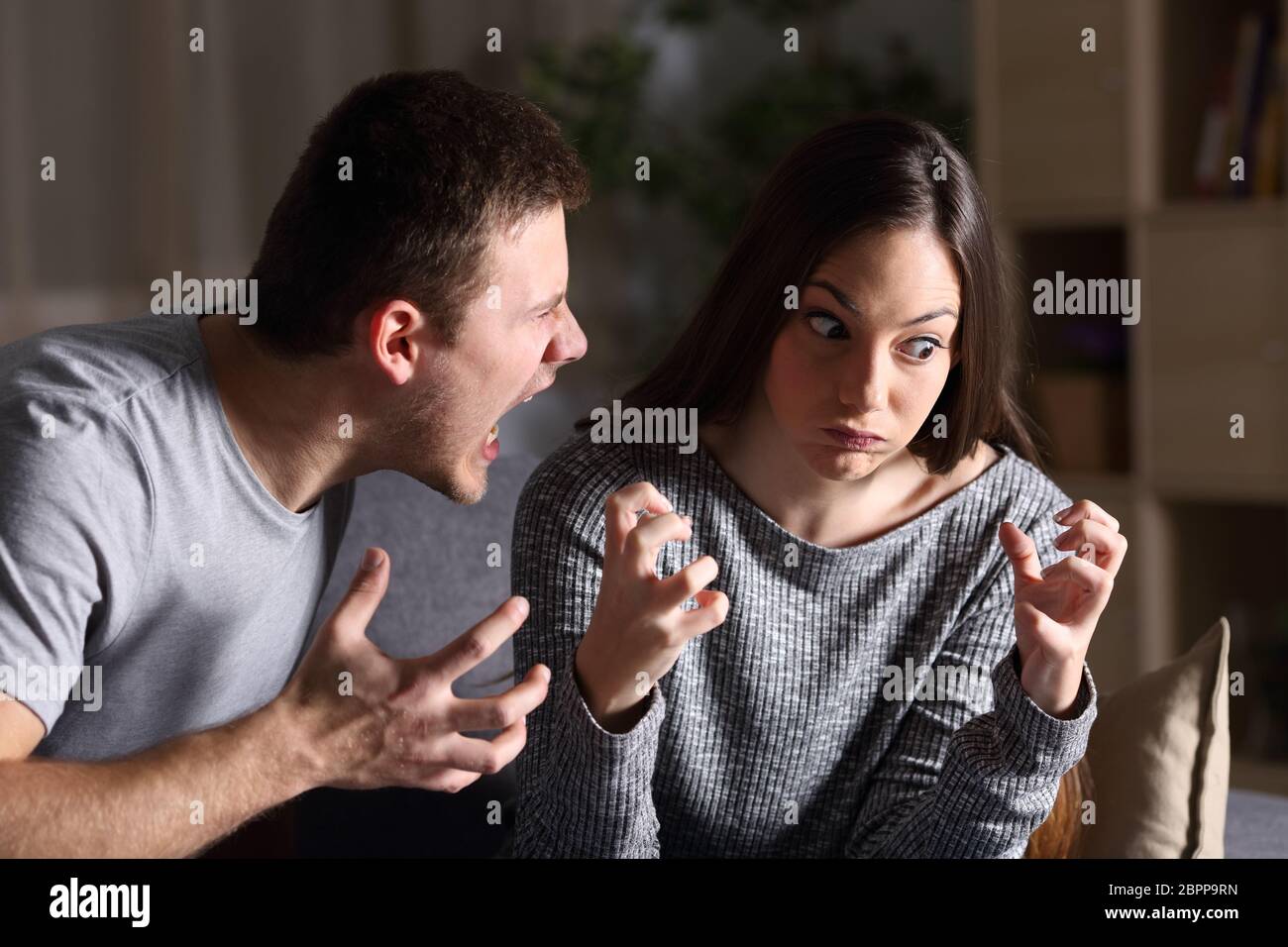 Couple arguing and shouting sitting on a couch in the living room at ...