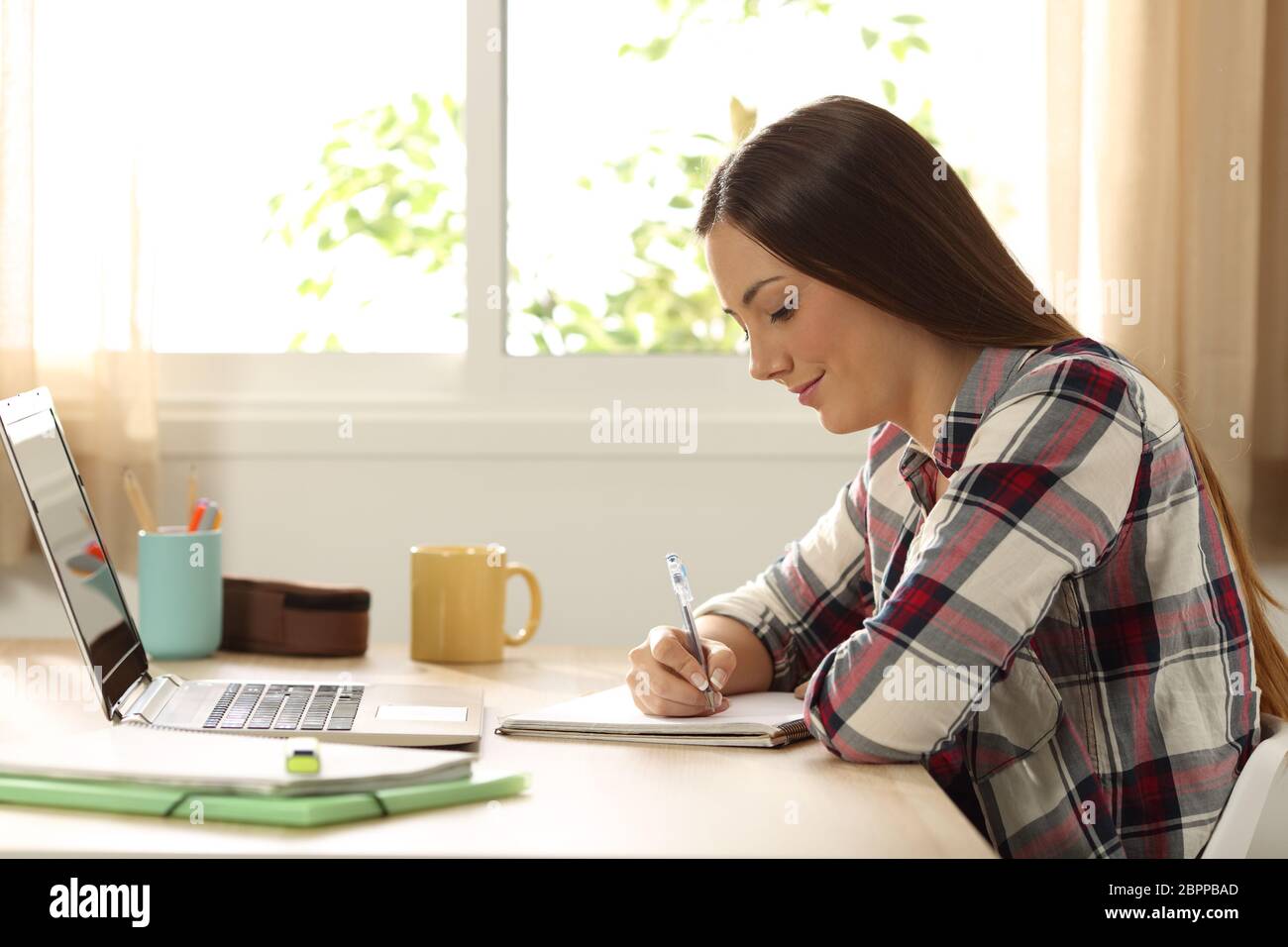 Side view of a single student studying and taking notes in a table at ...