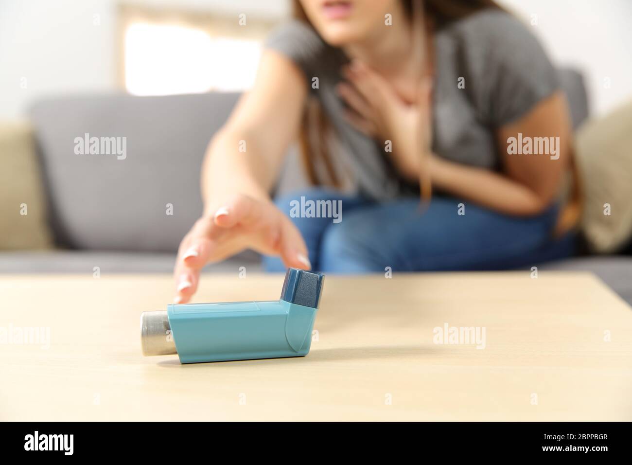 Girl suffering asthma attack reaching inhaler sitting on a couch in the ...