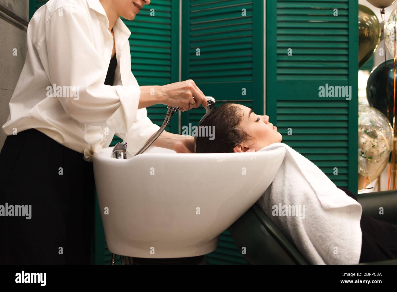 Beautiful young girl washes her head in a beauty studio. Hairdresser is ...